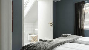 Um quarto com uma cama, uma janela com cortinas, uma porta e vista para um banheiro.