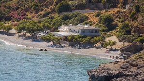 Uma propriedade costeira com praia, terreno rochoso e um edifício com vários níveis e telhado plano.