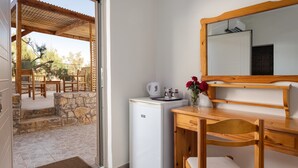Quarto compacto com parede de pedra, escrivaninha de madeira, geladeira branca e um pequeno espaço de estar com mesa e cadeiras.