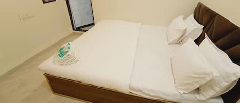 Cama bem arrumada com lençóis brancos, cabeceira marrom e uma toalha pequena na peseira.