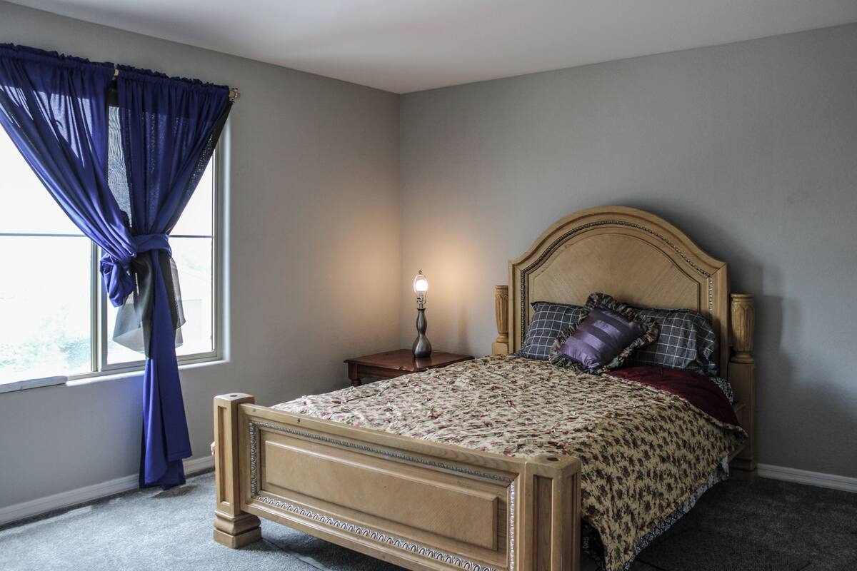 Um quarto com cama de madeira, mesa de cabeceira, luminária e janela com cortinas.