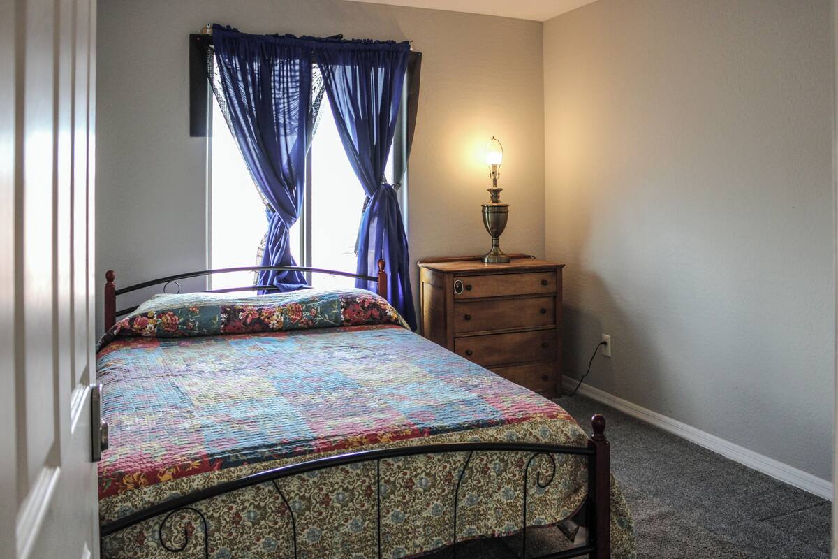 Quarto com cama, penteadeira, abajur e janela com cortinas.