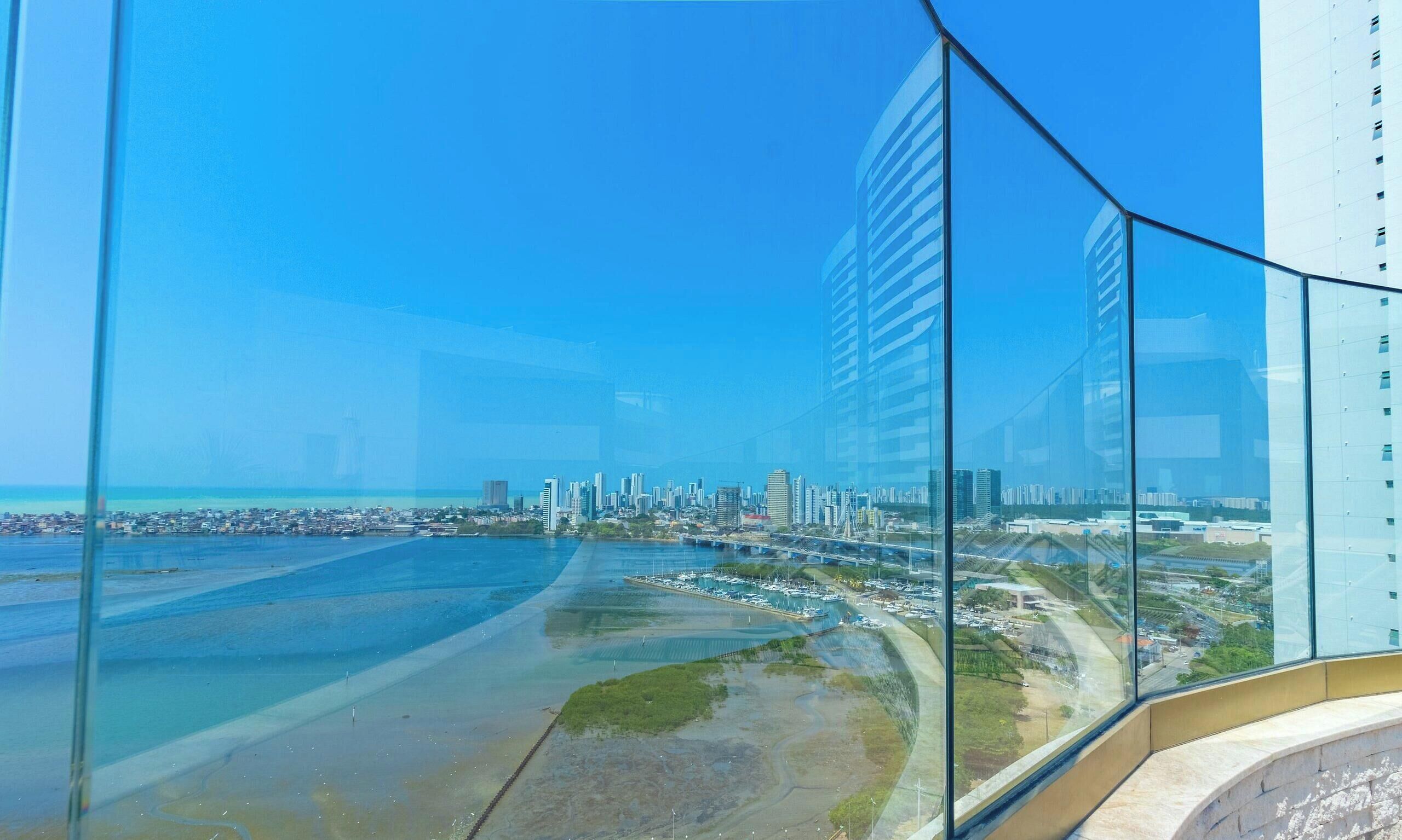 Um edifício alto com vista para o horizonte costeiro, incluindo um porto de iates e uma ponte.