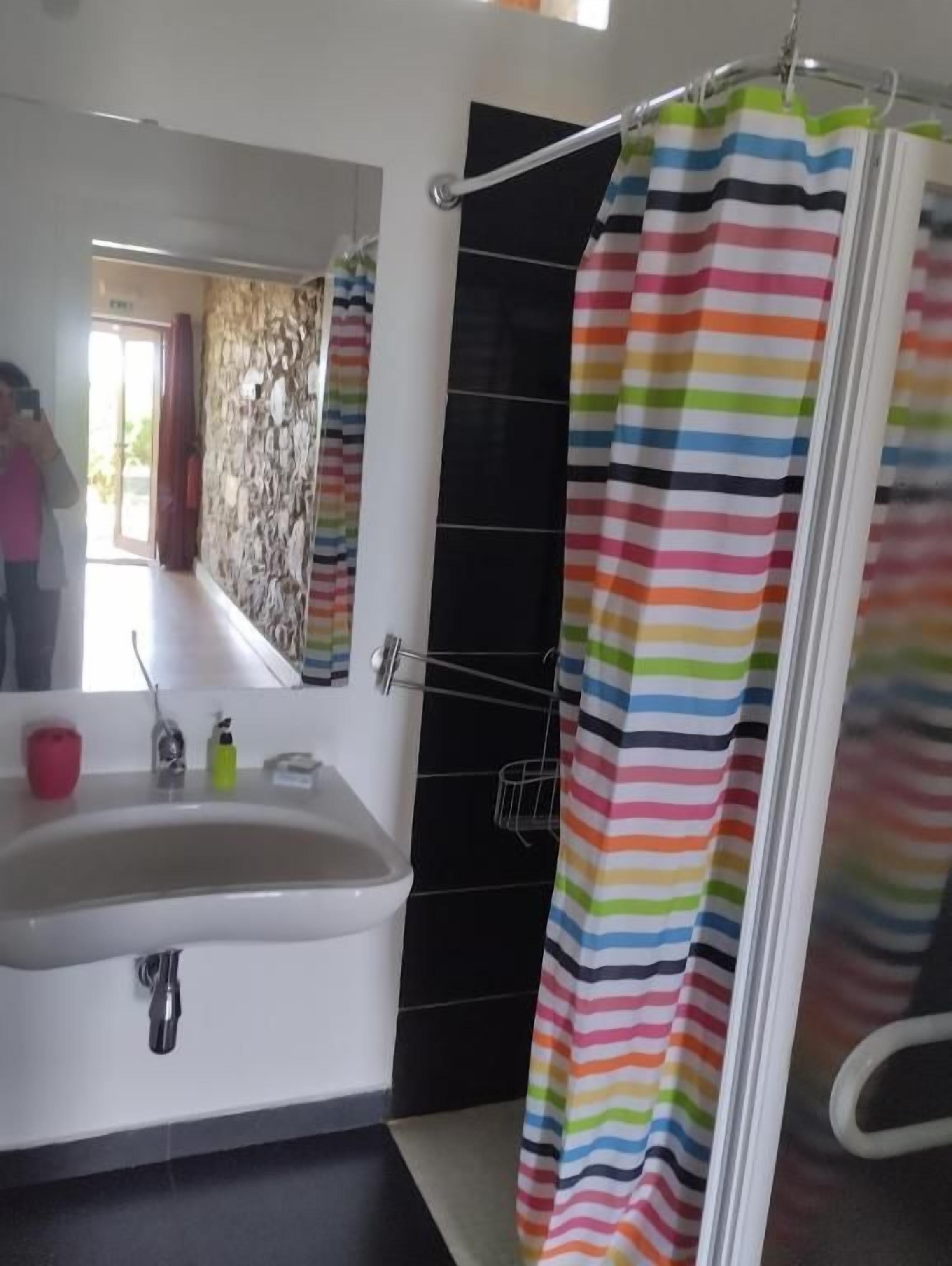 Casa de banho com uma pia branca, espelho e cortina de chuveiro com listras coloridas.