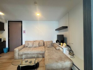 Uma sala de estar com sofá, mesa de centro de vidro, televisão e prateleira fixa com objetos.