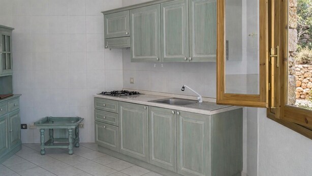 Uma cozinha com armários verde-claros, um fogão a gás, uma pia e uma pequena mesa de madeira.