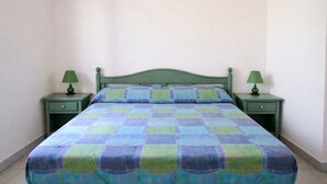Uma cama com colcha xadrez, duas mesas de cabeceira com abajures e cabeceira verde.