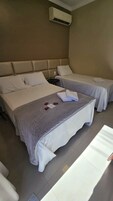 Quarto de hotel com duas camas, cabeceira, unidade de ar condicionado e mesa de cabeceira com abajur.
