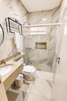 Um banheiro com piso de mármore, chuveiro com divisória de vidro, vaso sanitário e pia com porta-toalhas.