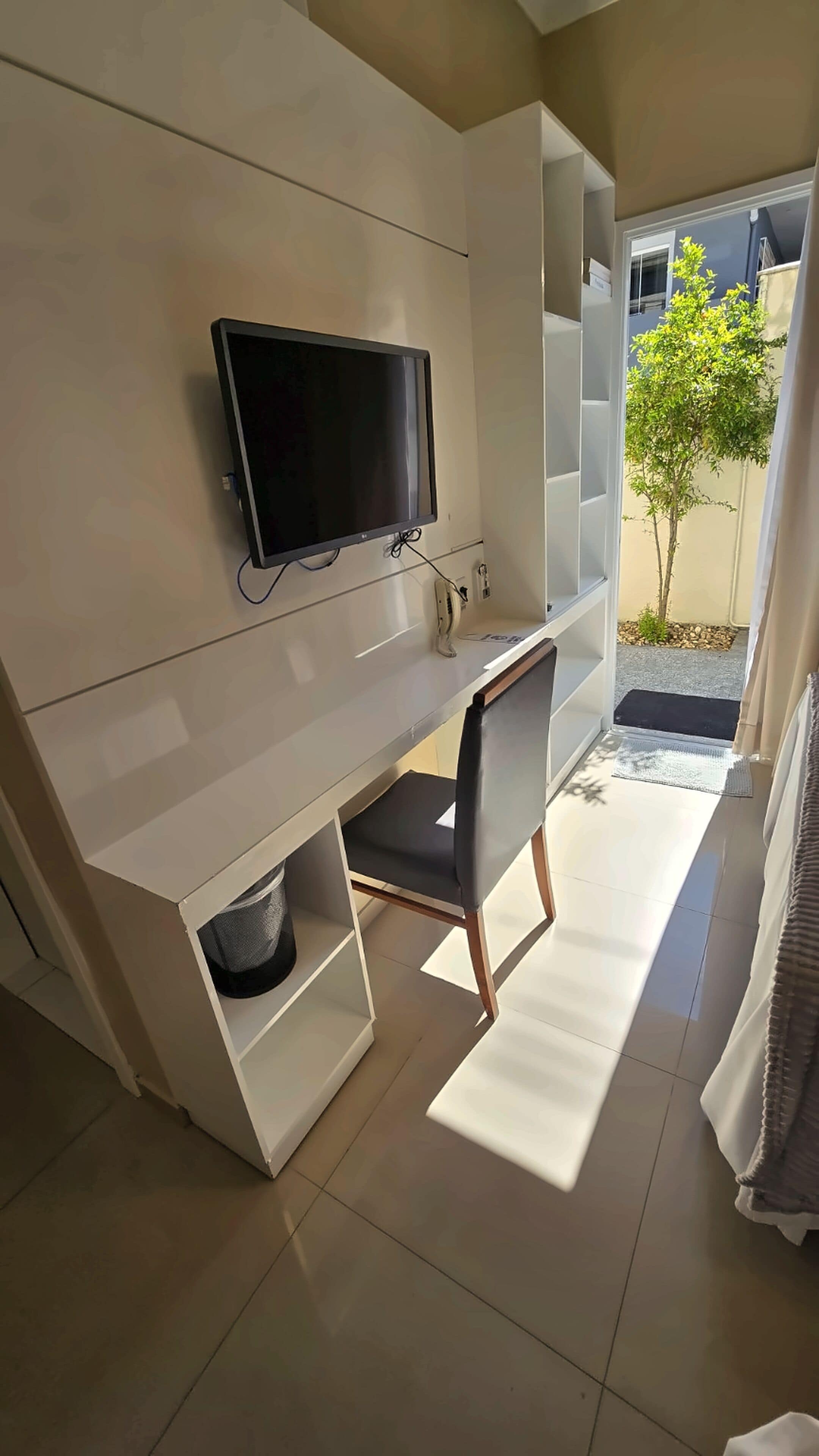 Quarto moderno com escrivaninha embutida, televisão de tela plana e uma cadeira.