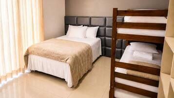 Quarto de hotel com uma cama, uma beliche de madeira e uma grande janela com cortinas.