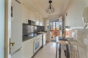 Uma cozinha com armários brancos, bancada preta, forno embutido e um espaço de refeições com mesa e cadeiras.