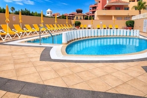 Piscina com cadeiras de sol amarelas e guarda-sóis, em volta de um deck revestido com azulejos.