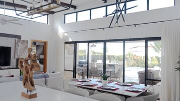 Ampla sala de estar com mesa de jantar posta para quatro pessoas, grandes janelas e design moderno no teto.