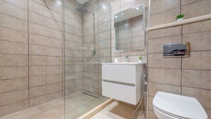 Uma casa de banho moderna com cabine de duche em vidro, lavatório branco e sanita.
