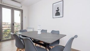 Uma sala de jantar moderna com uma mesa e cadeiras cinzas, um quadro na parede e vista pela porta de vidro.