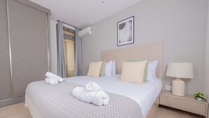 Quarto de hotel com cama, mesa de cabeceira, abajur e ar-condicionado fixado na parede.