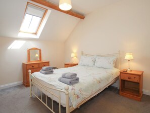 Quarto com cama, duas mesas de cabeceira, penteadeira, cômoda, espelho e claraboia.