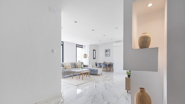 Uma sala de estar moderna com piso de mármore, um conjunto de sofás, uma mesa de centro e um vaso decorativo.