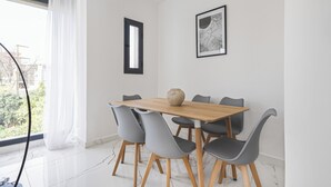 Uma área de refeições com uma mesa de madeira e cadeiras cinzentas, um vaso na mesa e uma obra de arte emoldurada na parede.