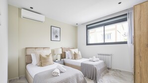 Quarto de hotel com duas camas, janela com vista, ar condicionado e radiador.