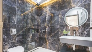 Um banheiro moderno com chuveiro em cabine de vidro, vaso sanitário branco e painel de fundo de mármore.
