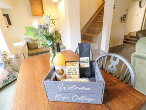 Uma mesa de madeira com uma placa de 'Welcome Hope Cottage', uma garrafa de suco de laranja, uma caixa de chá e uma garrafa de vinho.