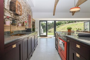 Cozinha moderna com armários escuros, parede decorada com pedra e uma grande janela com vista para um jardim.