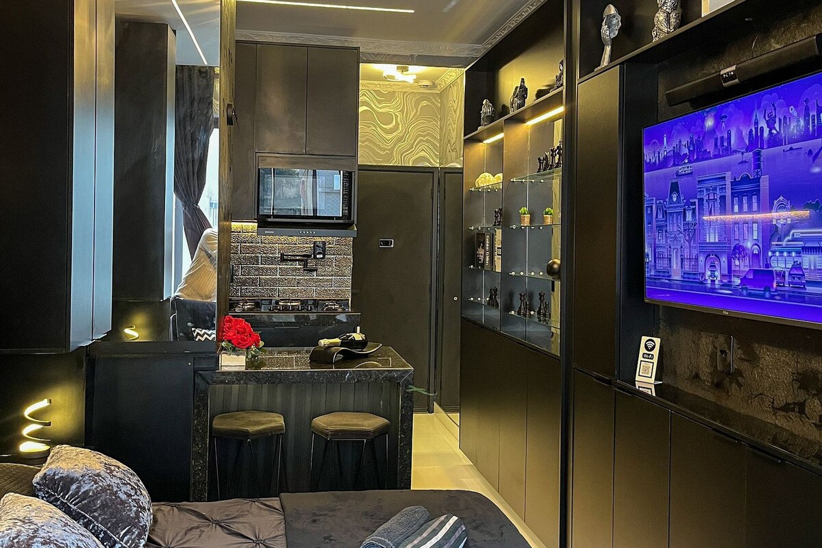 Quarto de hotel moderno com uma cama grande, televisão, minibar e lustre.