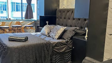 Quarto moderno com cama grande, um sofá, uma TV e vista para prédios.
