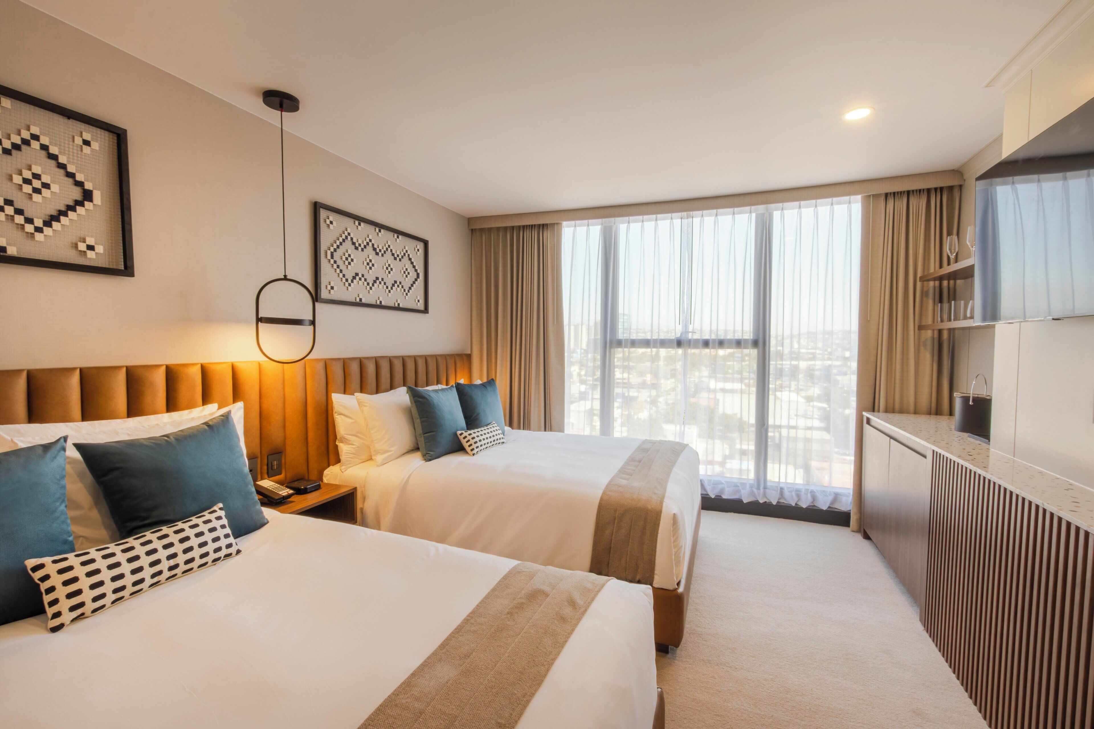 Quarto de hotel com duas camas, uma janela grande, minibar e vista para a cidade.