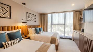 Quarto de hotel com duas camas, uma janela grande, minibar e vista para a cidade.