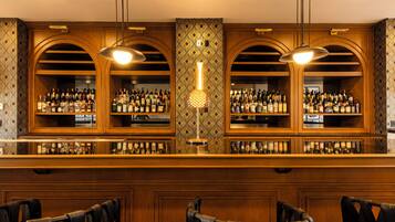 Uma área de bar com armários de madeira, prateleiras cheias de garrafas e duas luminárias pendentes.