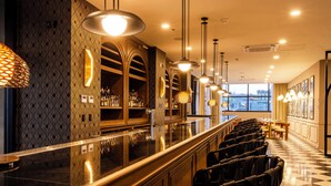 Uma área de bar com um balcão comprido, várias luminárias pendentes e chão quadriculado.