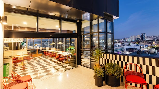 Um edifício moderno com piso xadrez, área externa para sentar e grandes janelas com vista para a cidade.