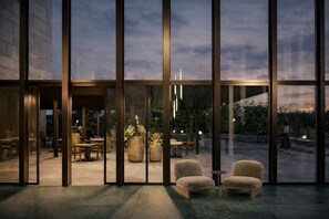 Um interior moderno com grandes janelas de vidro, uma área de estar com cadeiras e um pátio exterior visível.