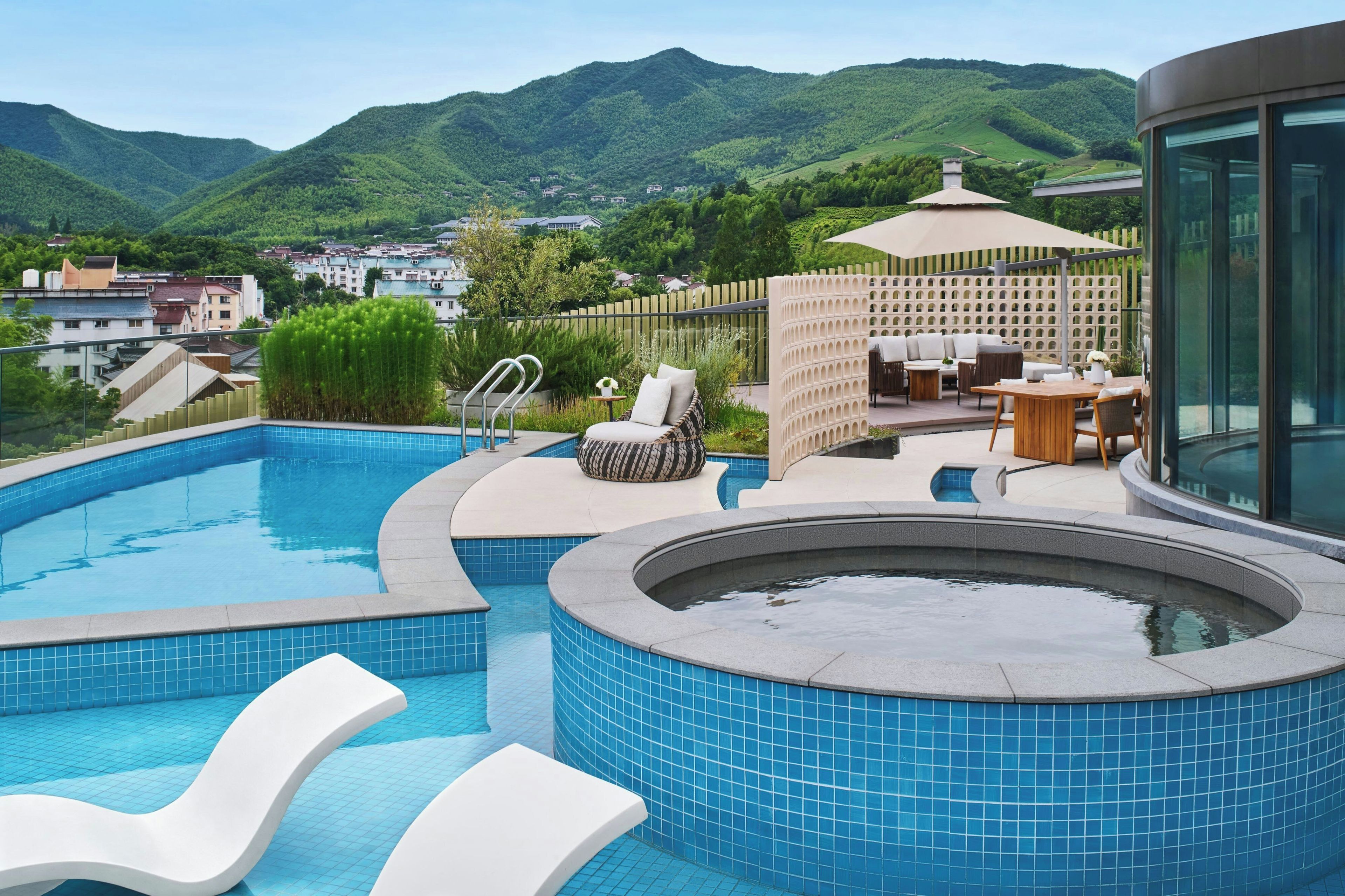 Piscina com banheira de hidromassagem, área de estar e vista para montanhas.