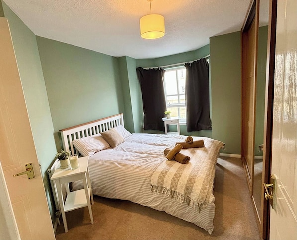Quarto com cama, mesa de cabeceira e janela com cortinas.