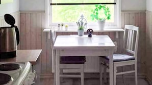 Uma cozinha com uma mesa e cadeira brancas, uma janela com vista e uma chaleira no fogão.