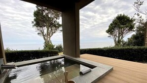 Uma banheira de hidromassagem com deck de madeira, rodeada por árvores e vista para o mar.