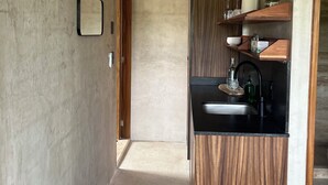 Um corredor estreito com porta de madeira e uma pequena área de cozinha, com pia e prateleiras.