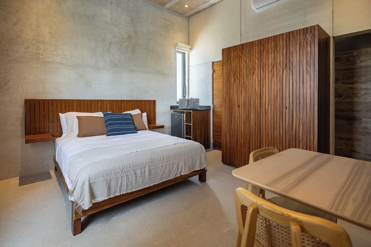 Um quarto com uma cama de madeira, uma mesinha e uma cadeira.