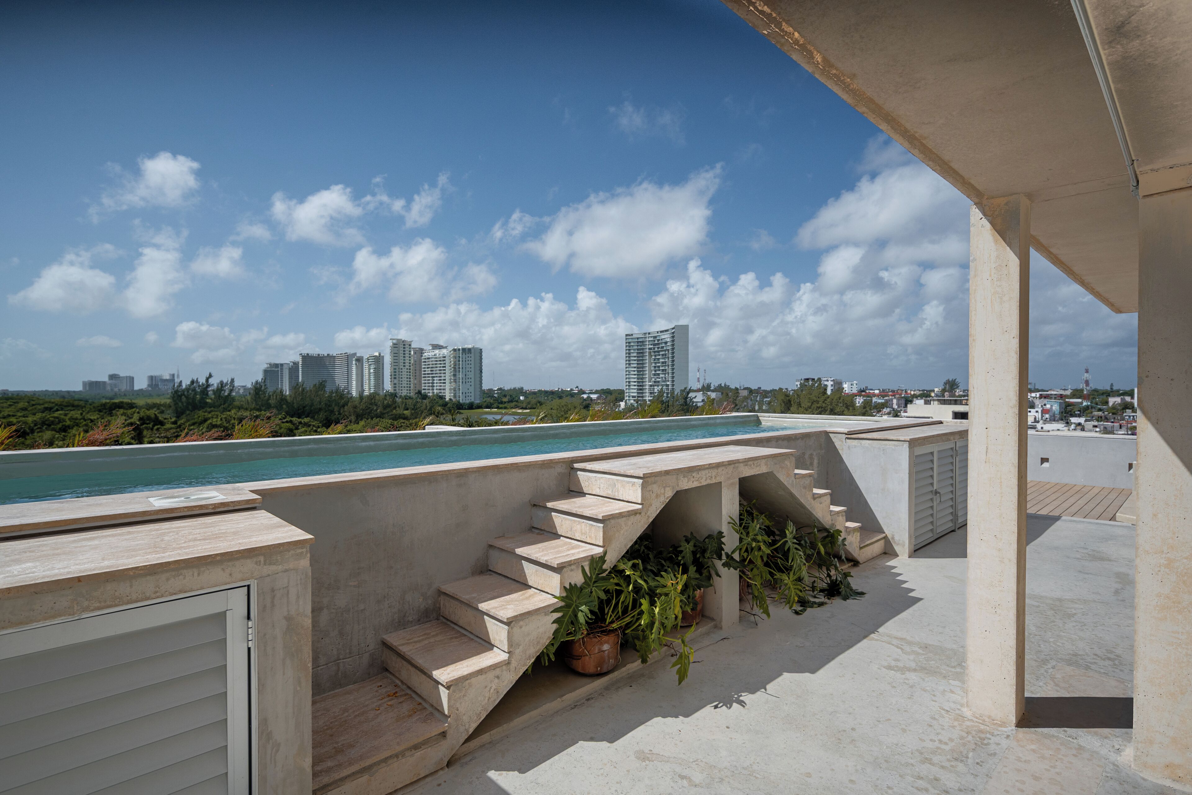 Piscina no terraço com vista para o horizonte urbano, degraus de concreto e plantas em vasos.