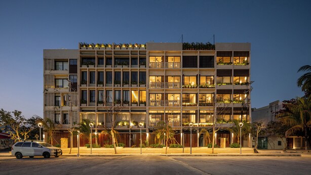 Um hotel com vários andares, varandas, iluminação externa e um carro estacionado em frente.