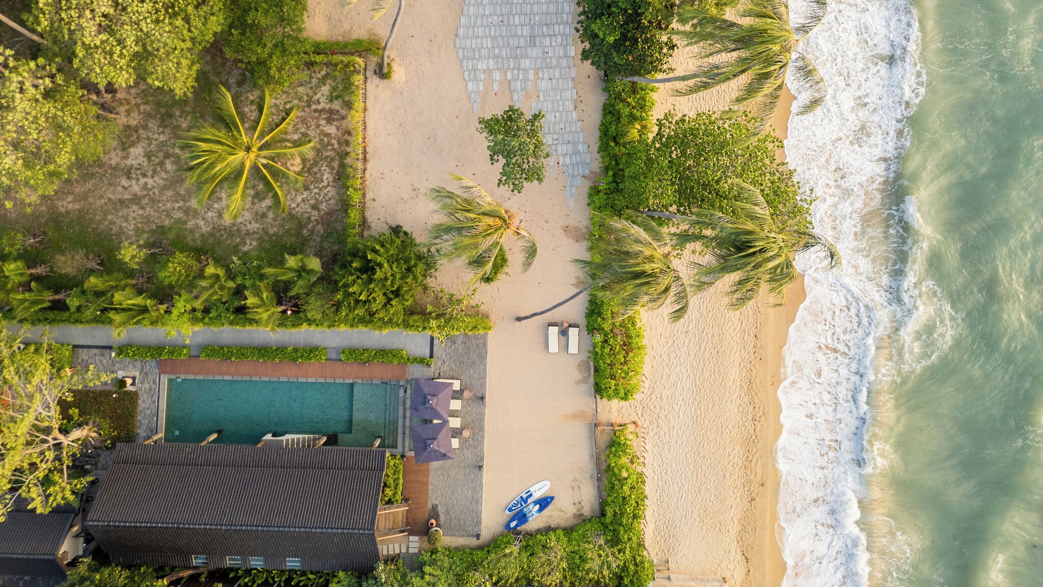 Vista aérea de uma propriedade à beira-mar com piscina, espreguiçadeiras e área de praia.