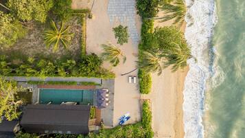 Vista aérea de uma propriedade à beira-mar com piscina, espreguiçadeiras e área de praia.