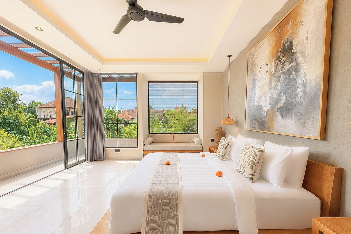 Quarto espaçoso com uma cama grande, vista para o verde lá fora e um ventilador de teto.