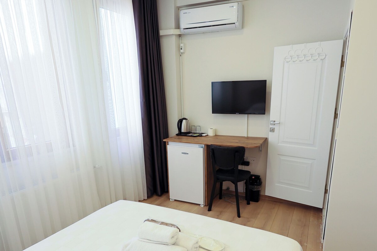 Quarto de hotel com cama, escrivaninha, computador, televisão e ar condicionado.