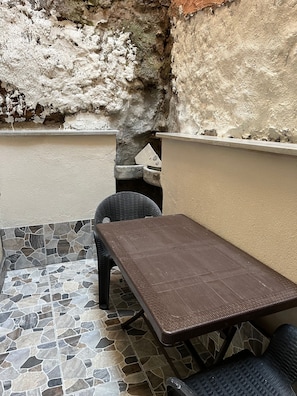 Uma área de pátio com mesa e cadeiras, piso de pedra e parede texturizada.