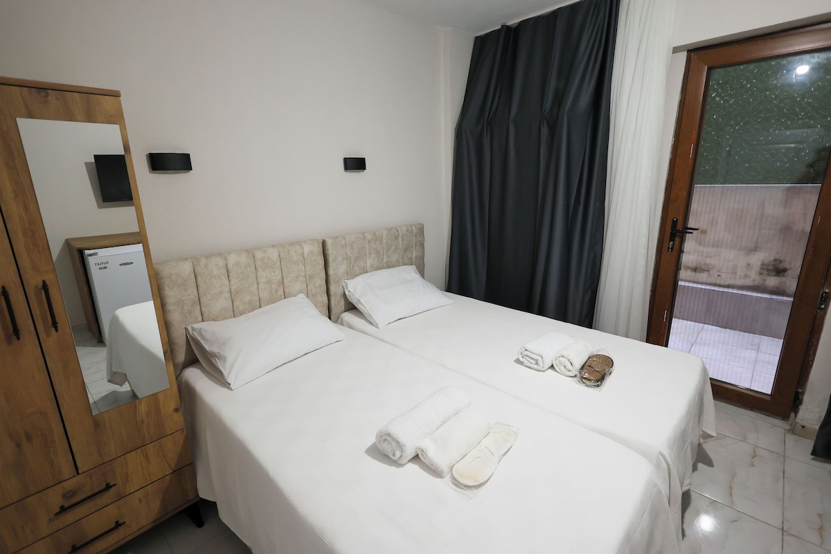 Quarto de hotel com duas camas, um guarda-roupa, um espelho e uma porta de vidro deslizante para o exterior.